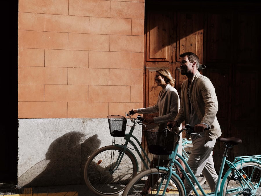 Uma pessoa andando de bicicleta passando por um edifício com parede de tijolos e porta de madeira.