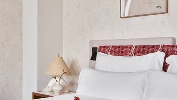 Cama bem arrumada com lençóis brancos, um cobertor de tricô vermelho e uma luminária em uma mesa de cabeceira.