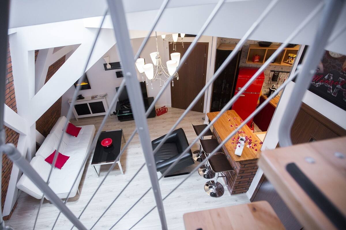 Interior moderno com sofá branco, almofadas vermelhas, uma cadeira preta, mesa de madeira e um armário vermelho.