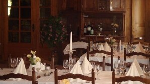 Uma sala de jantar com mesas de madeira preparadas para uma refeição, com toalhas de mesa brancas e velas.
