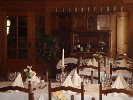 Uma sala de jantar com mesas de madeira preparadas para uma refeição, com toalhas de mesa brancas e velas.