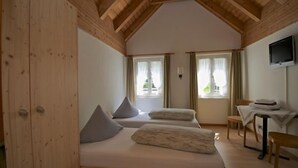 Quarto com duas camas, uma mesa pequena, uma TV e vigas de madeira no teto.