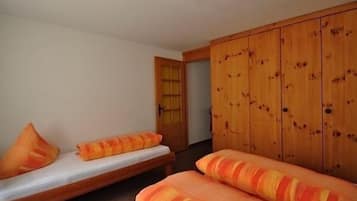 Quarto com duas camas, guarda-roupa de madeira e porta que dá para outro espaço.