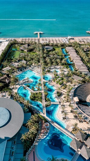 Vista aérea de um resort com uma grande piscina central, palmeiras e uma área de praia.
