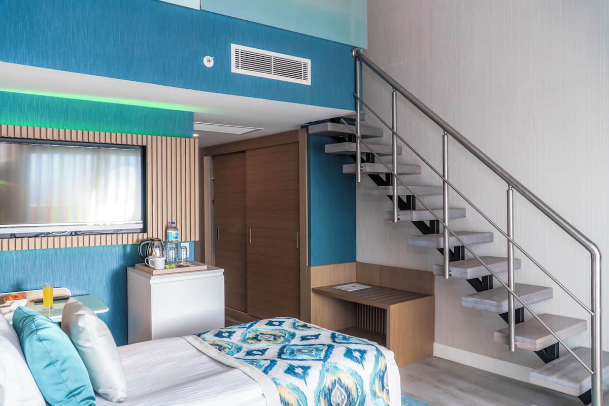 Quarto de hotel moderno com cama, escrivaninha, armário e escada.