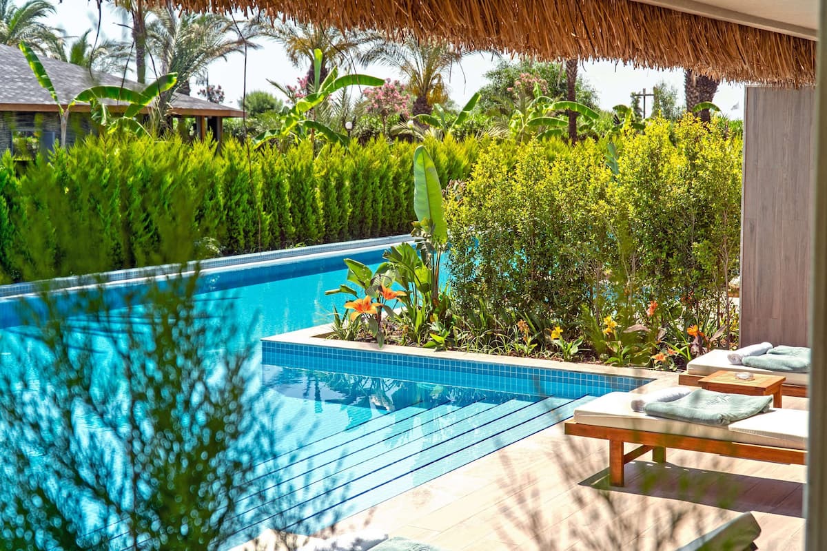 Piscina com espreguiçadeiras e estrutura de telhado de palha.