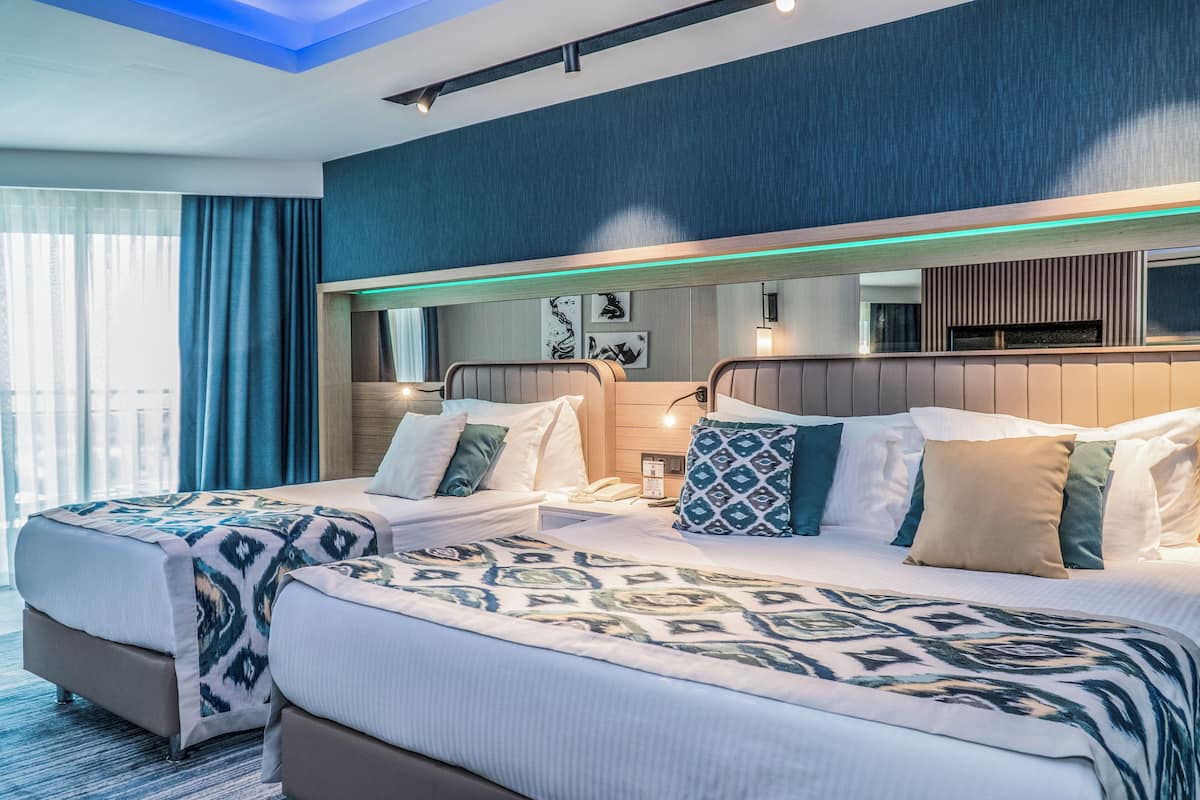 Quarto de hotel moderno com duas camas, um espelho grande e vista para a cidade.