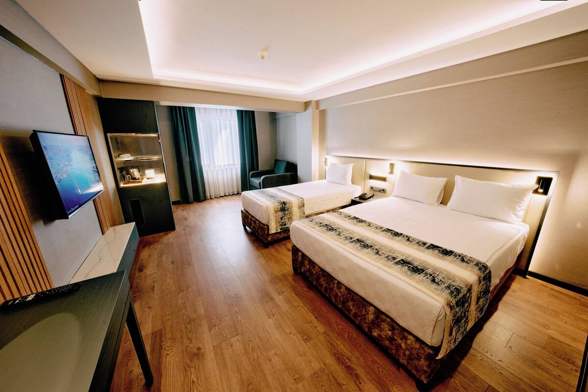 Quarto de hotel com duas camas, televisão, secretária e vista para a cidade.