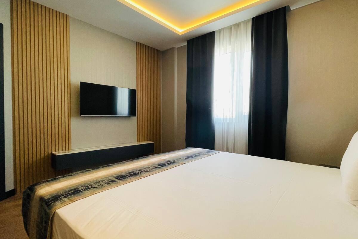 Quarto de hotel com uma cama grande, uma televisão de tela plana na parede e uma janela com cortinas.