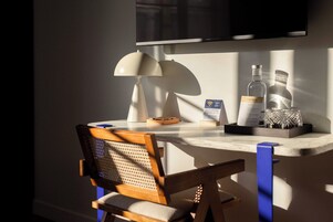 Quarto moderno com escrivaninha, cadeira, luminária, garrafa e televisão de tela plana fixada na parede.