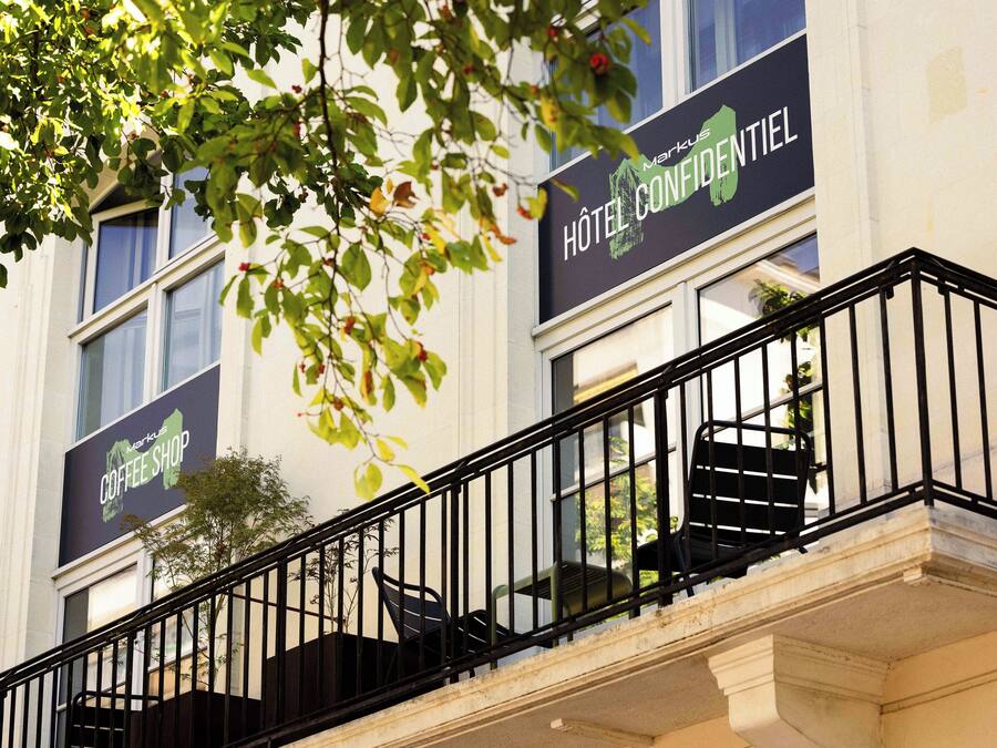 Um hotel com varandas, um letreiro de cafeteria e uma placa com 'Hôtel Confidentiel'.