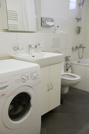 Um banheiro moderno com máquina de lavar frontal, pia, vaso sanitário e chuveiro.