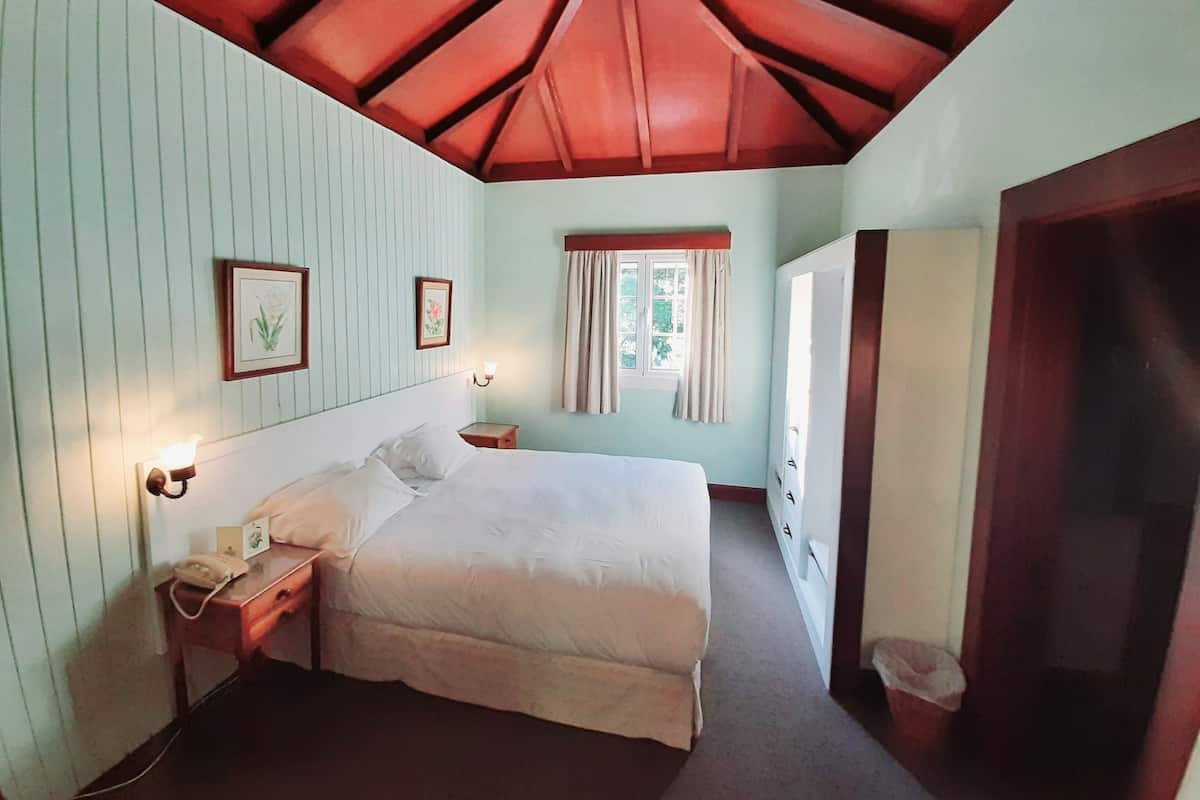 Quarto com cama, mesas de cabeceira, telefone, quadros emoldurados, janela com cortinas e porta.