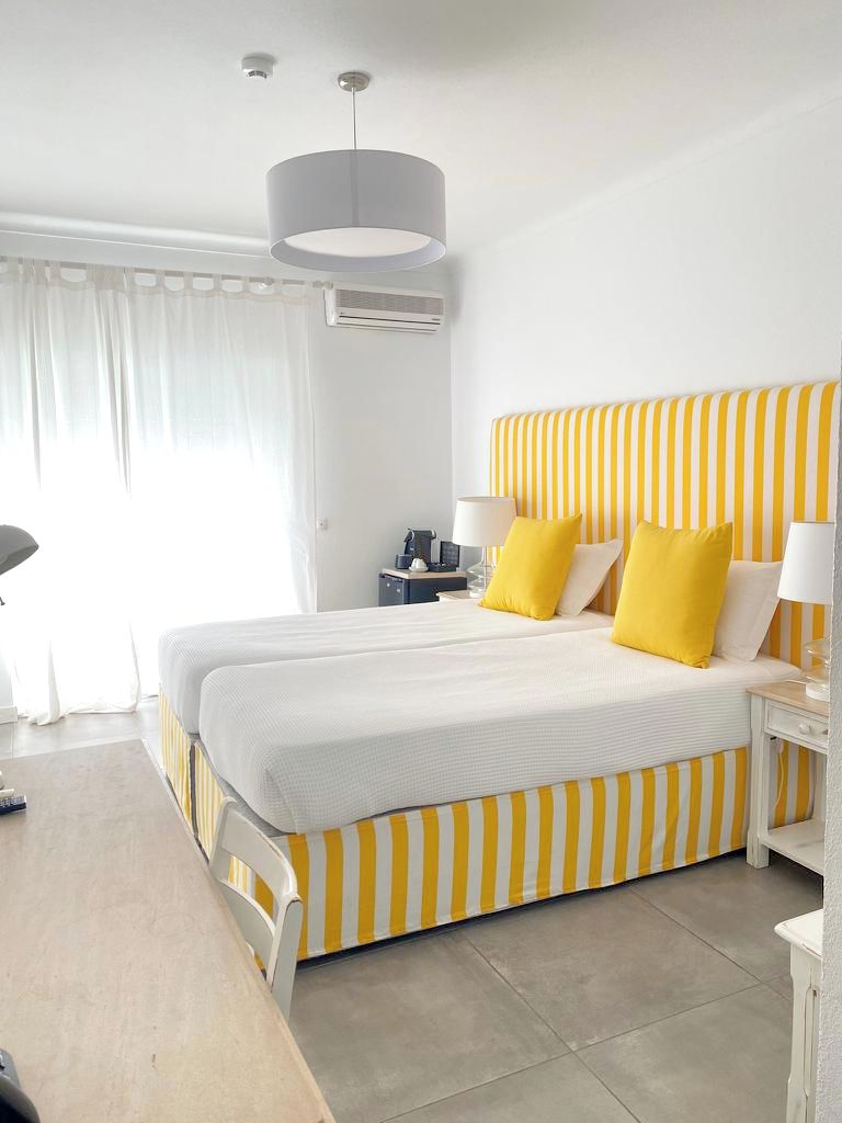 Quarto de hotel com uma cama grande, mesas de cabeceira, uma escrivaninha e uma cadeira.