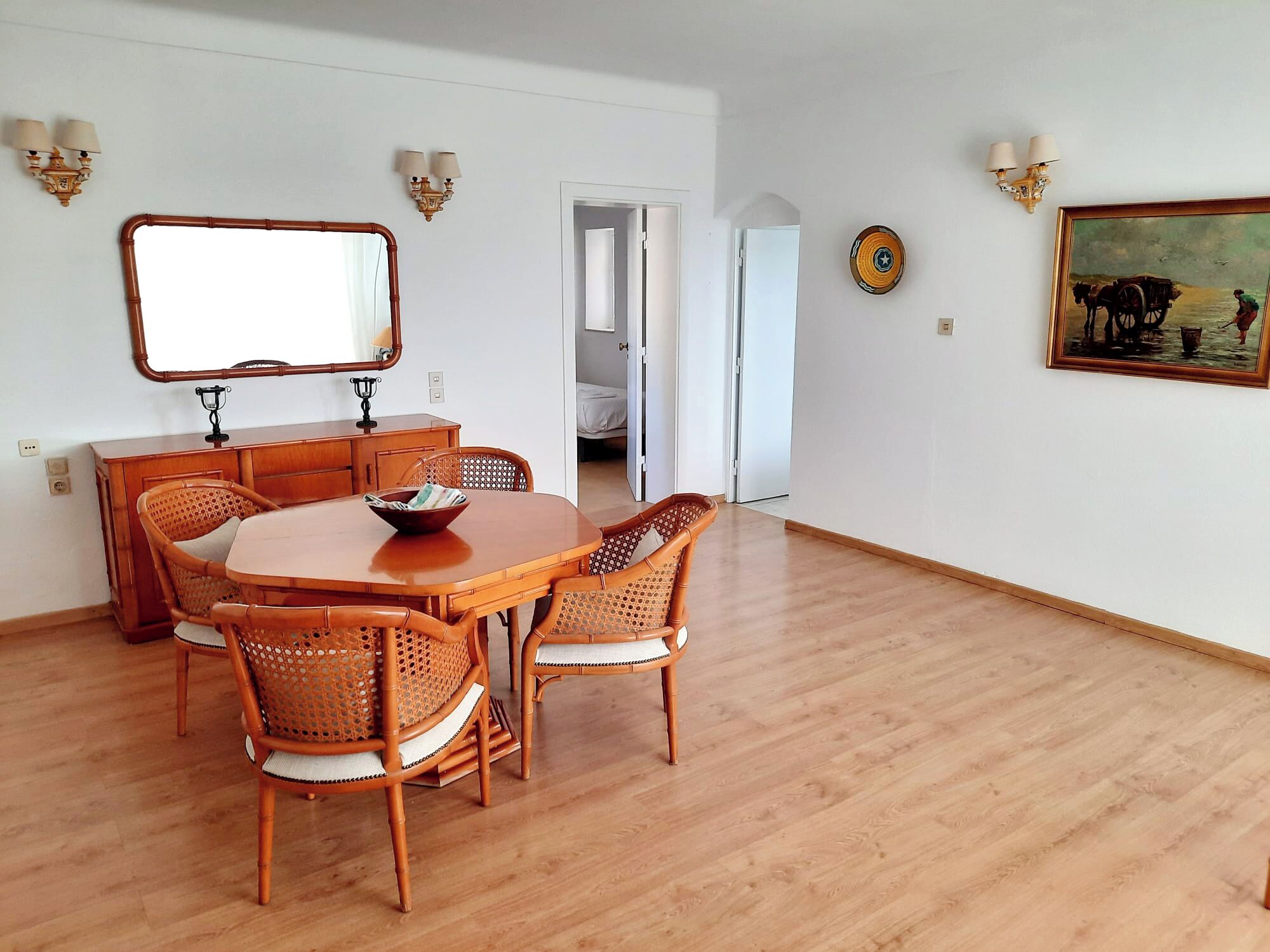 Uma área de refeições com uma mesa e cadeiras de madeira, um espelho, arandelas e um quadro.