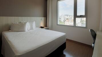 Quarto de hotel com uma cama grande, uma escrivaninha e uma janela com vista para a cidade.