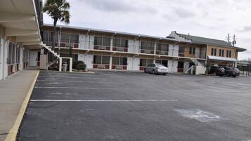 Um motel com estacionamento, uma escadaria que leva à entrada e uma palmeira.