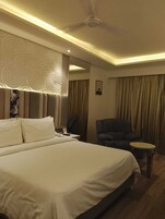Quarto de hotel com uma cama grande, uma escrivaninha, uma cadeira, uma mesinha e um ventilador de teto.
