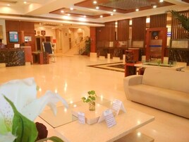 Um hall de hotel com balcão de recepção, escada, área de estar e balcão de atendimento.
