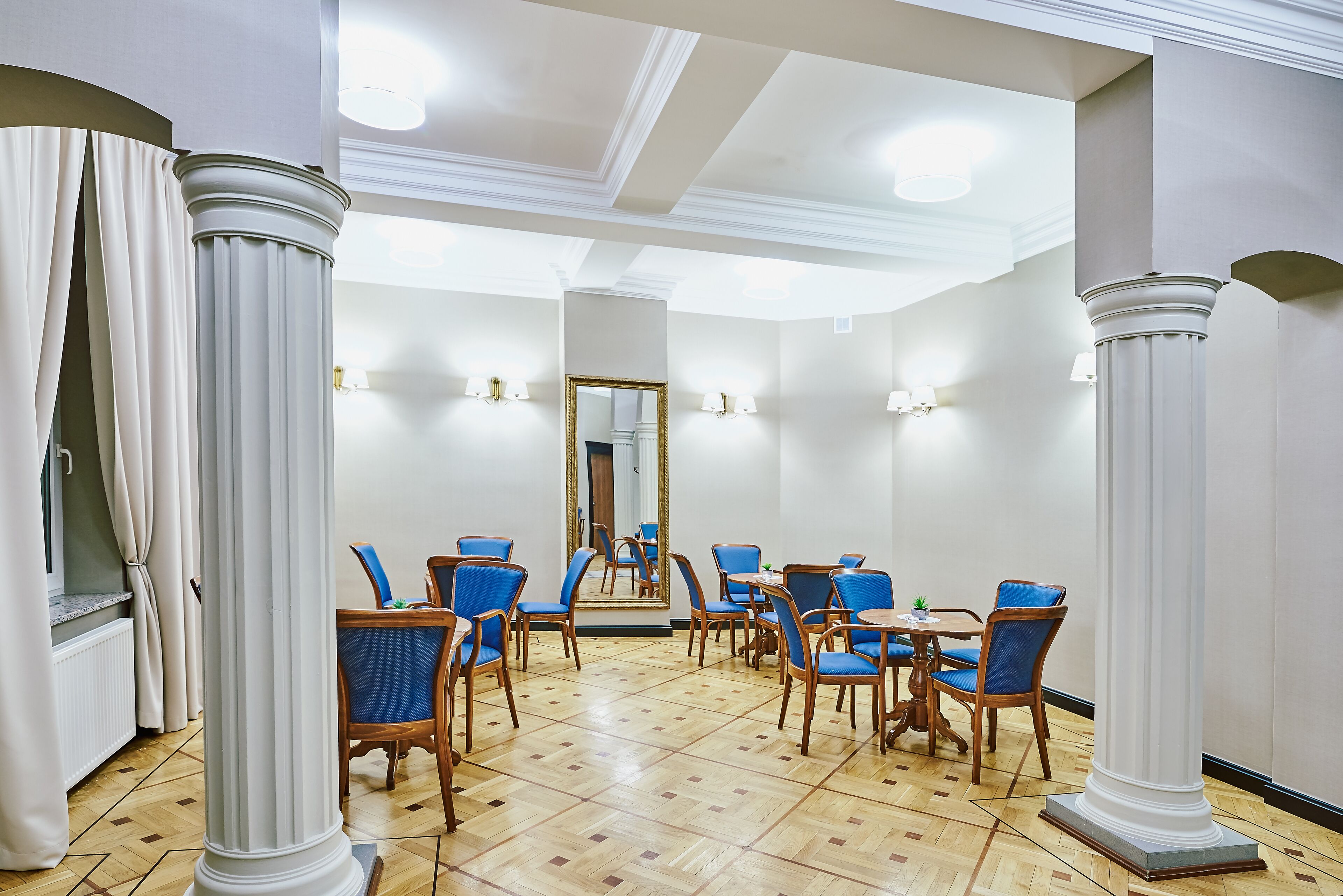 Um quarto com piso de madeira polida, colunas brancas e cadeiras azuis dispostas ao redor de mesas.