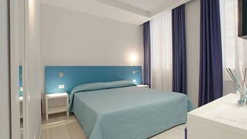 Quarto com cama, mesas de cabeceira, escrivaninha e secretária com abajur.