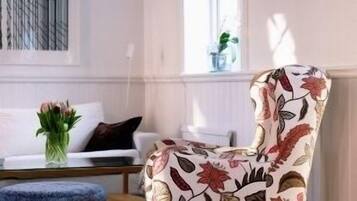Uma sala de estar moderna com um sofá branco, uma poltrona floral, uma mesa de centro de madeira e um banquinho azul.