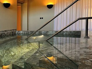 Interior moderno com escadaria de mármore, arandelas e piso refletivo.
