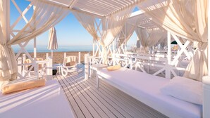Uma cabana à beira-mar com móveis brancos, incluindo um sofá e cadeiras, e um deck de madeira.