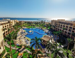Um resort com uma piscina grande central, várias varandas e vista para o mar.