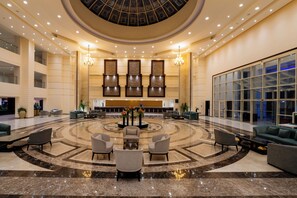 Um hall amplo com área de estar central, balcão de recepção e um grande painel de vidro.
