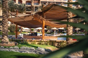 Uma pérgola de madeira com área de piscina, espreguiçadeiras e guarda-sóis.