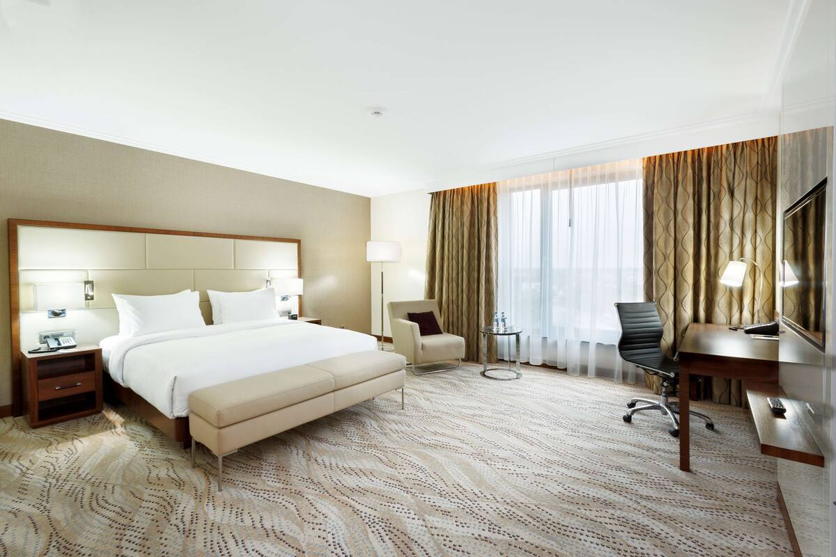 Quarto de hotel com uma cama grande, mesas de cabeceira, escrivaninha, uma cadeira e televisão.