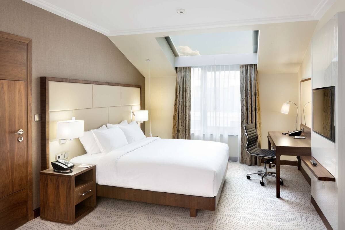 Quarto de hotel com uma cama grande, uma escrivaninha, uma cadeira, uma televisão e um guarda-roupa.