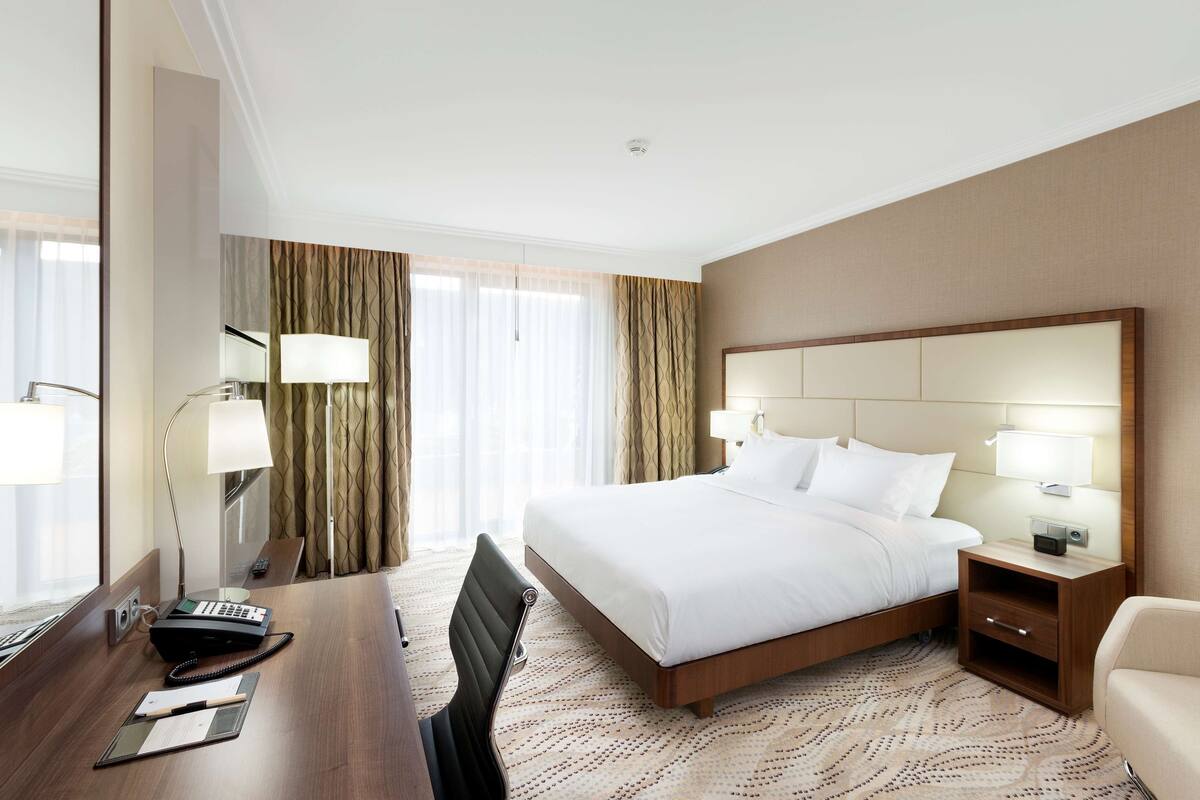 Quarto de hotel com uma cama grande, luminárias de cabeceira, uma escrivaninha com telefone e uma cadeira.