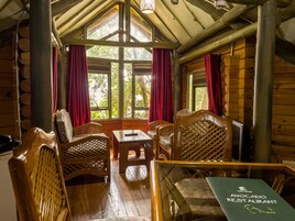 Interior acolhedor de uma cabana com paredes de madeira e uma grande janela. Há cadeiras de vime e uma mesa com um menu.