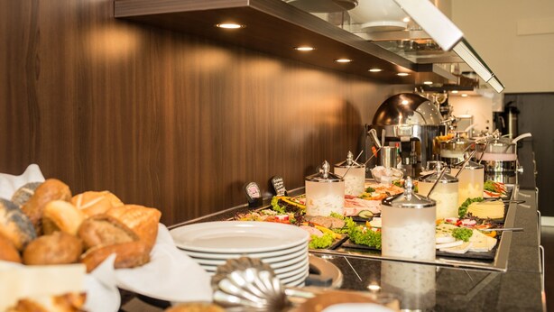Buffet montado com diversos alimentos e bebidas, incluindo pão, saladas e pratos quentes, em uma cozinha moderna.