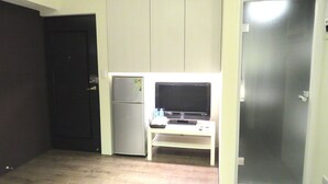 Uma pequena cozinha compacta com geladeira, micro-ondas e televisão em um suporte branco.