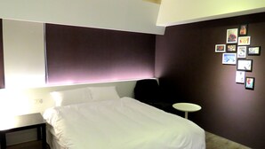 Quarto de hotel com cama, uma mesa pequena e parede com quadros.