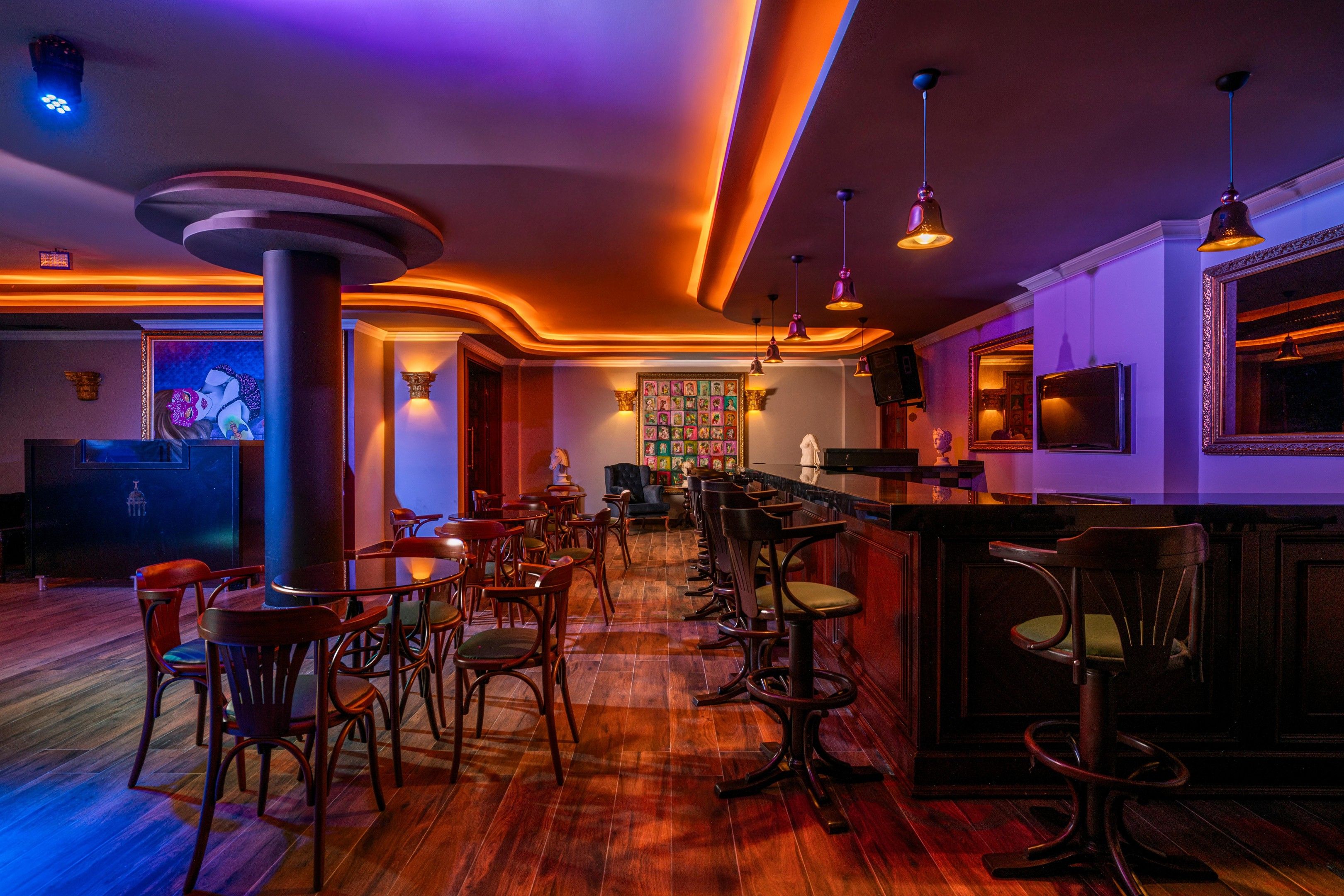Uma área de bar com piso de madeira, banquetas e iluminação pendente.