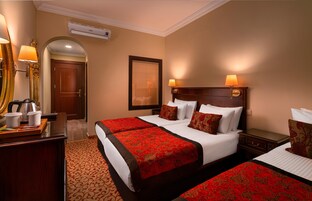 Quarto de hotel com cama de casal, mesa de cabeceira, luminária, espelho, guarda-roupa e ar condicionado.