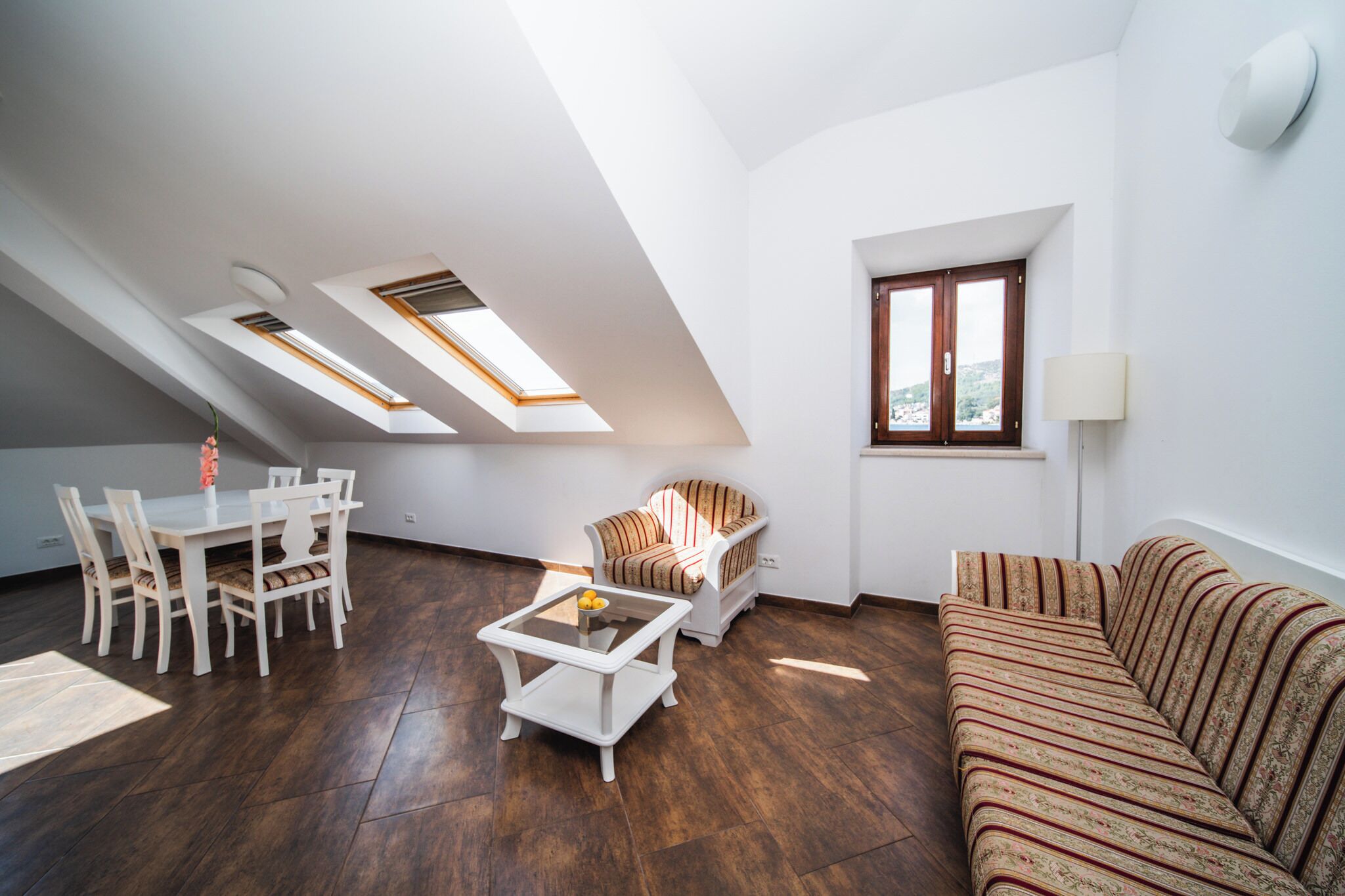 Uma sala de estar moderna com área de jantar, claraboias, sofá e poltrona.