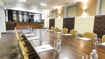 Sala de conferência com uma mesa comprida, cadeiras, garrafas de água e um painel de parede de tijolos.