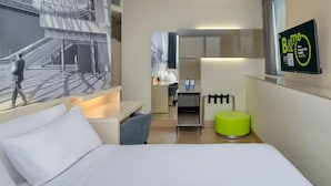 Quarto de hotel moderno com cama, um pequeno espaço de estar, uma escrivaninha e uma janela grande.