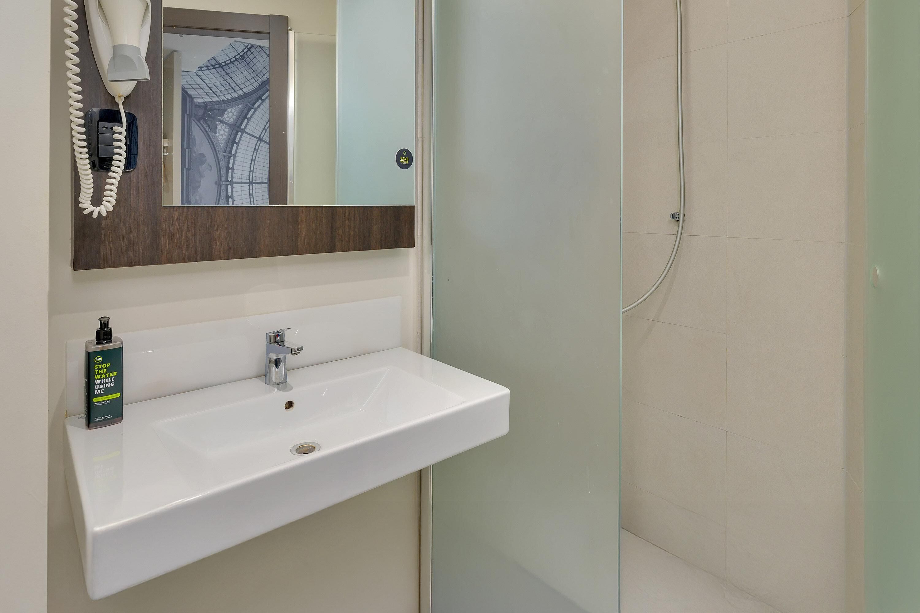 Casa de banho com lavatório branco, espelho, secador de cabelo e chuveiro.