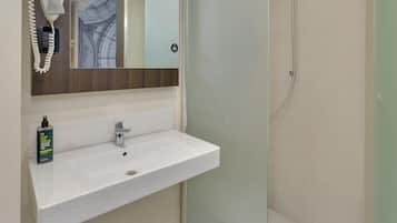 Casa de banho com lavatório branco, espelho, secador de cabelo e chuveiro.