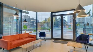 Interior moderno com sofá, duas poltronas e mesa de centro. Janelas amplas oferecem vista da cidade.