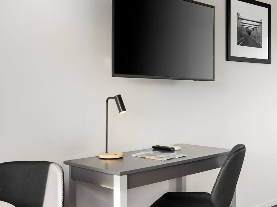 Quarto moderno com escrivaninha, duas cadeiras, televisão de tela plana, quadro emoldurado e luminária de mesa.