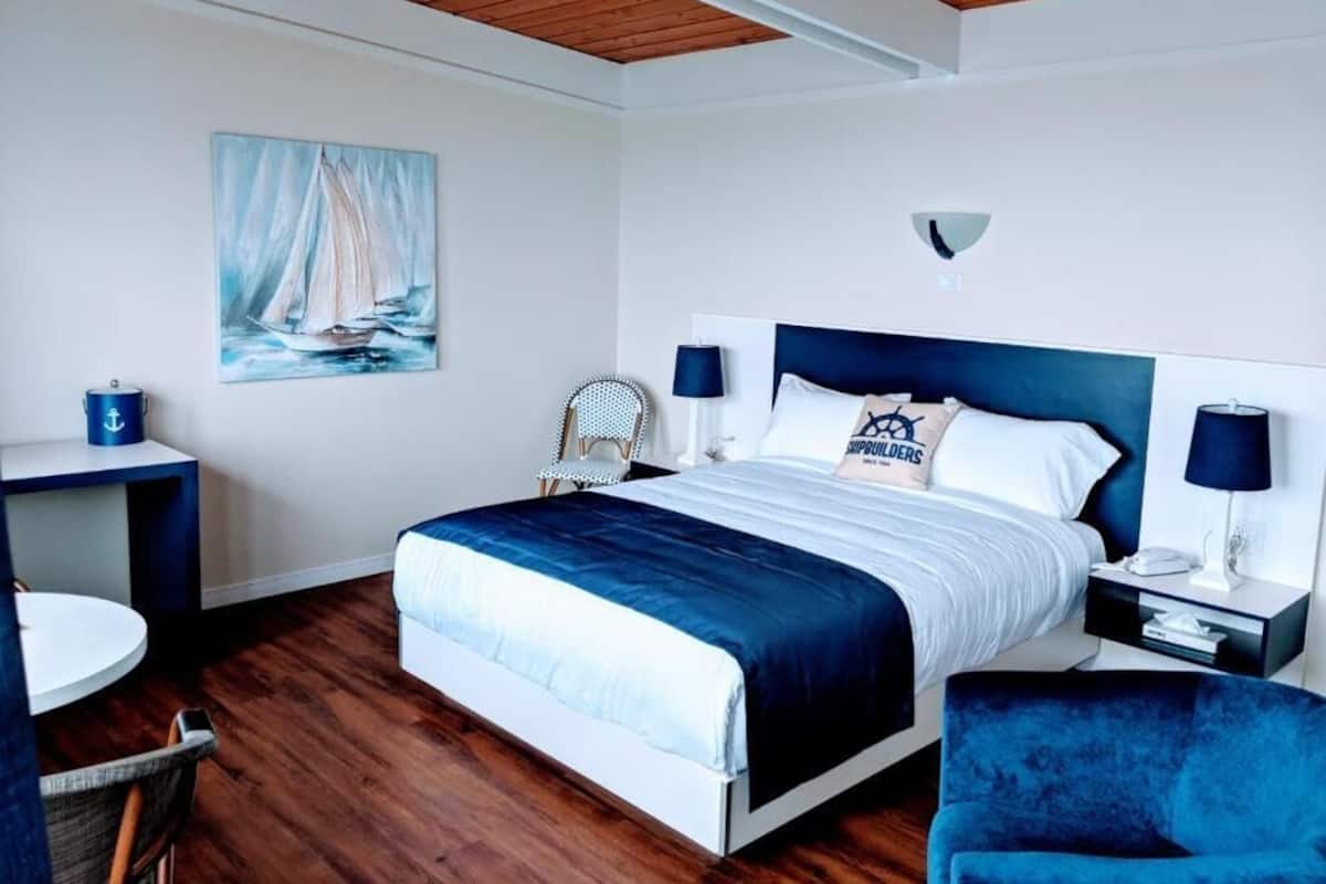 Quarto com cama, mesas de cabeceira, cadeira, escrivaninha, pintura e ventilador de teto.