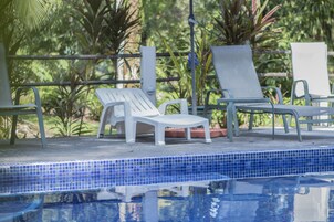 Uma área de piscina com espreguiçadeiras e borda revestida em azulejo.