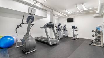 Uma academia com esteiras, elípticos e bolas de exercícios.